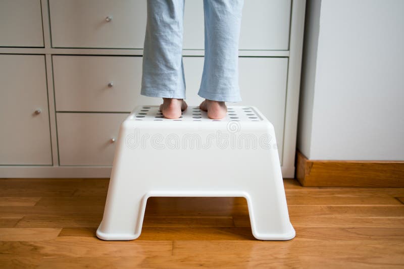 Child Standing on White Step Stool Reaching High Shelf in Home Setting ...