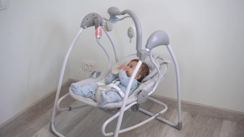 The Child Swings in the Cradle-swing and Eats Milk from a Bottle. a ...