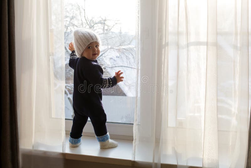 Child in a Warm Blue Jumpsuit is on Window in Winter Stock Photo ...