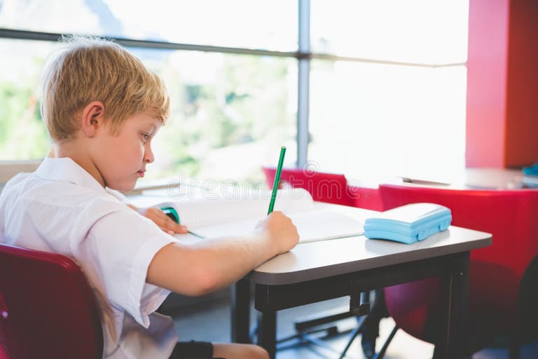 Child Writing in Notebook at White Desk in Classroom, with Blue Pencil ...