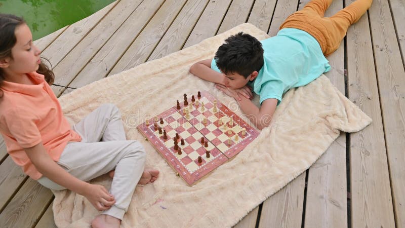 Two Children Enjoying a Game of Chess Outdoors on a Wooden Deck ...