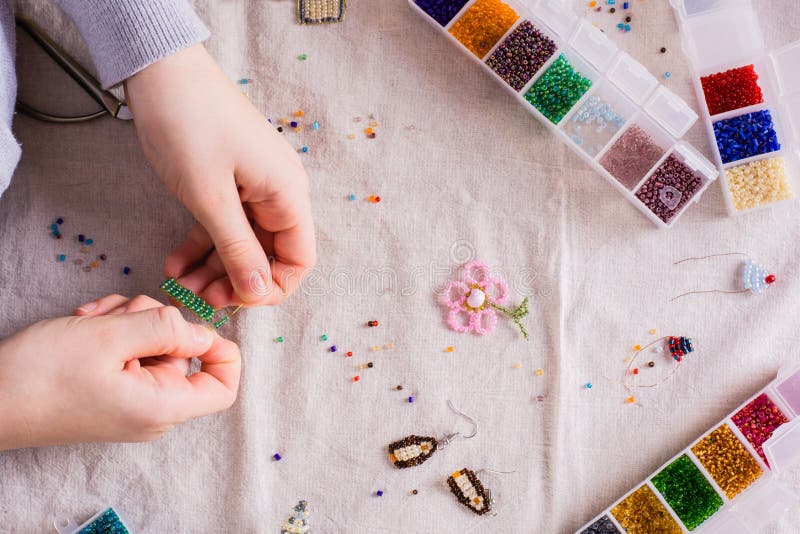 Children`s Hands Weave a Beaded Toy on a Table among Boxes with Beads ...
