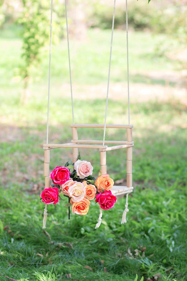 Children`s Rope Swing Hangs on a Tree in the Park. Roses Lie on a Swing ...