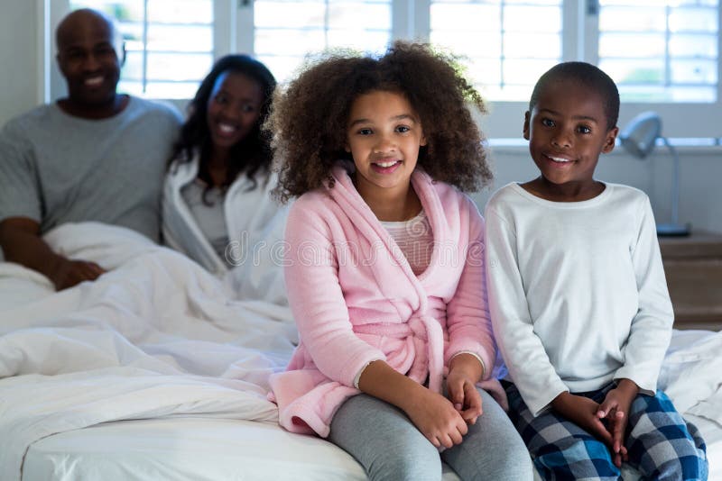 Children Sitting on Bed with Parents in Background Stock Image - Image ...