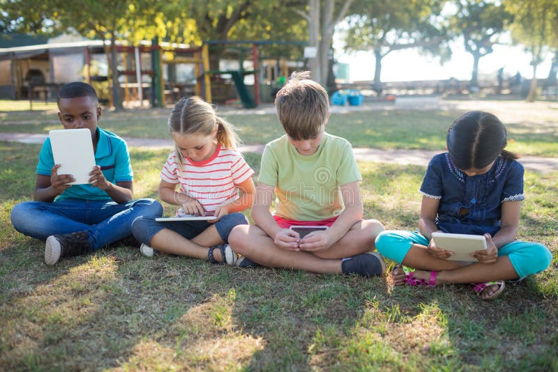 Children Using Tablet Computer while Sitting on Grassy Field Stock ...
