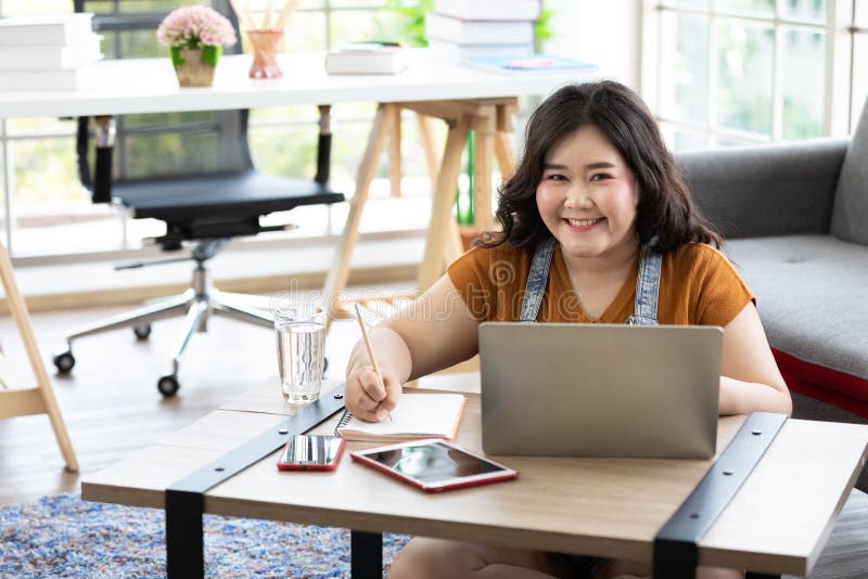 Chubby Woman Looking at Laptop Computer and Writing on Notebook for ...