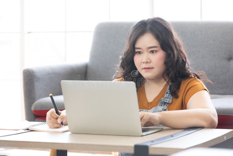 Chubby Woman Looking at Laptop Computer and Writing on Notebook for ...