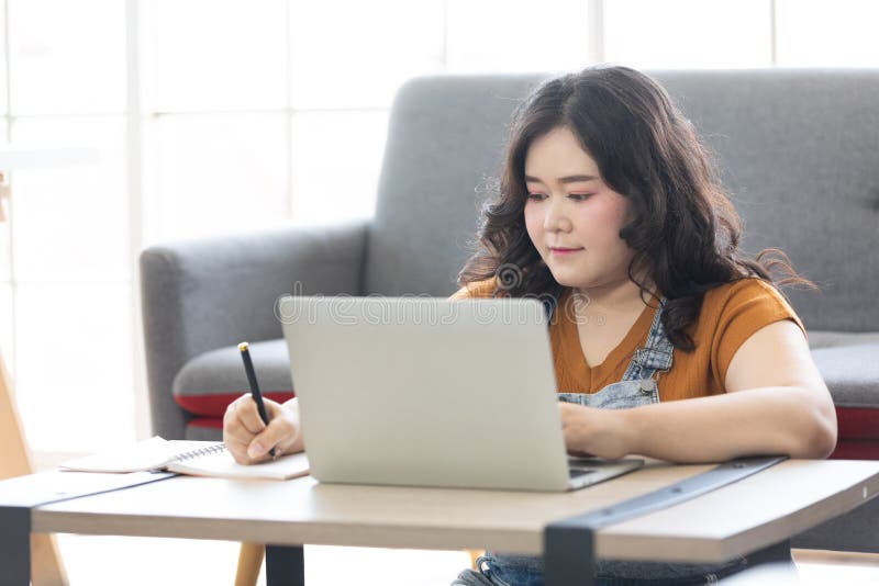 Chubby Woman Looking at Laptop Computer and Writing on Notebook for ...