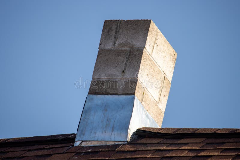 A Cinder Block Chimney on the Shingled Roof of a House with Clear Blue ...