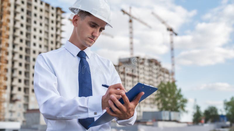 Civil Engineer in a White Helmet Makes Pencil Marks in the ...