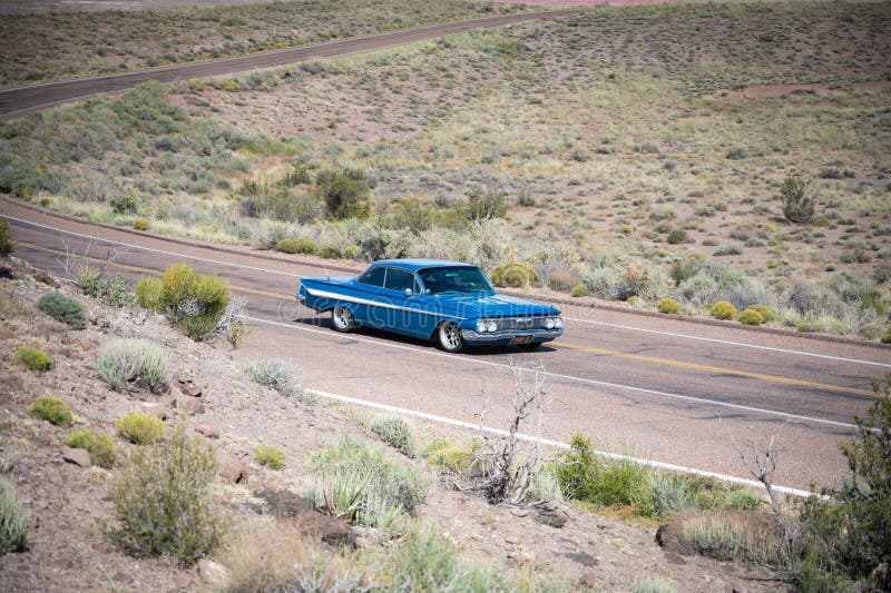 Classic Blue Car is Driving Down a Desert Highway, with Hills Visible ...