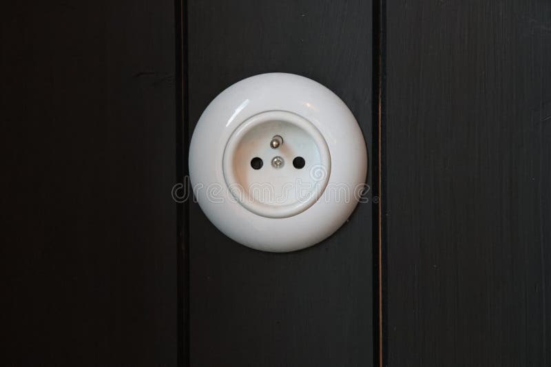 A Classic Round White Electrical Socket is Mounted on Vertical Black ...