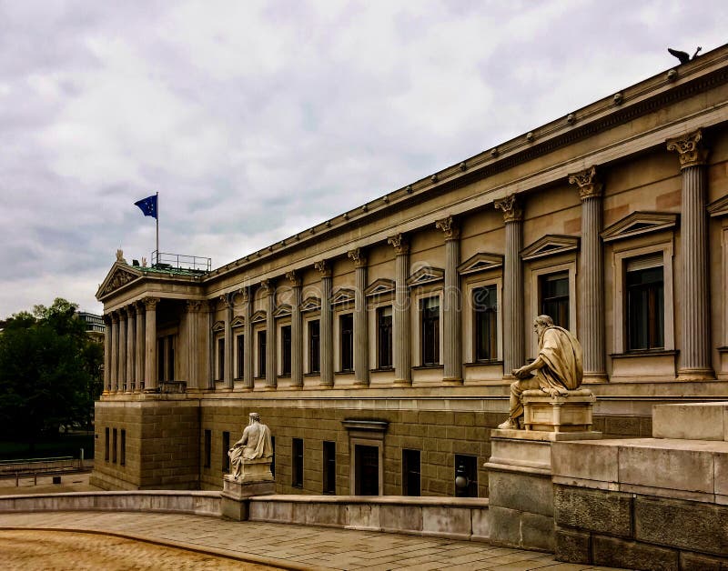 A Classical Building with Columns, Statues, and a Flag Under a Cloudy ...