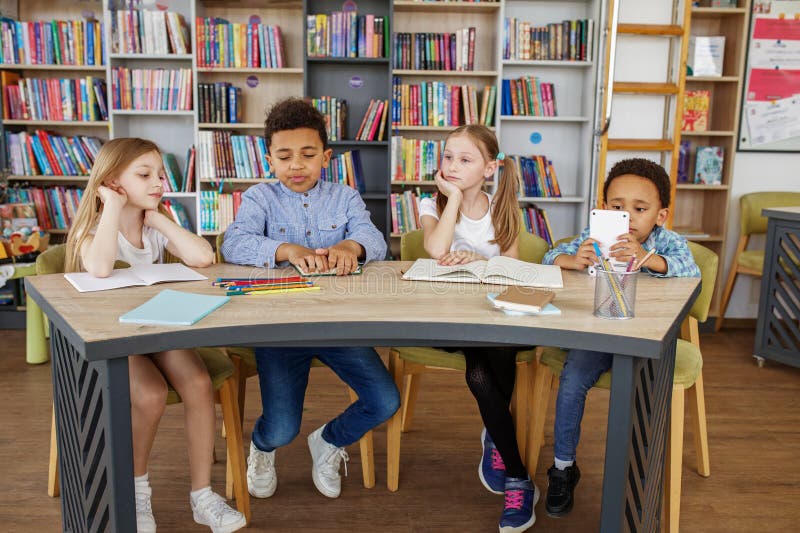 Multi-ethnic Pupils Study and Write at Table in Library or Classroom ...