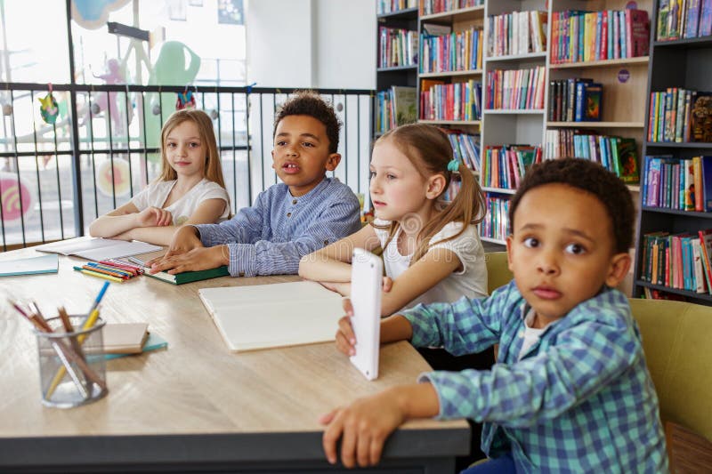 Multi-ethnic Pupils Study and Write at Table in Library or Classroom ...