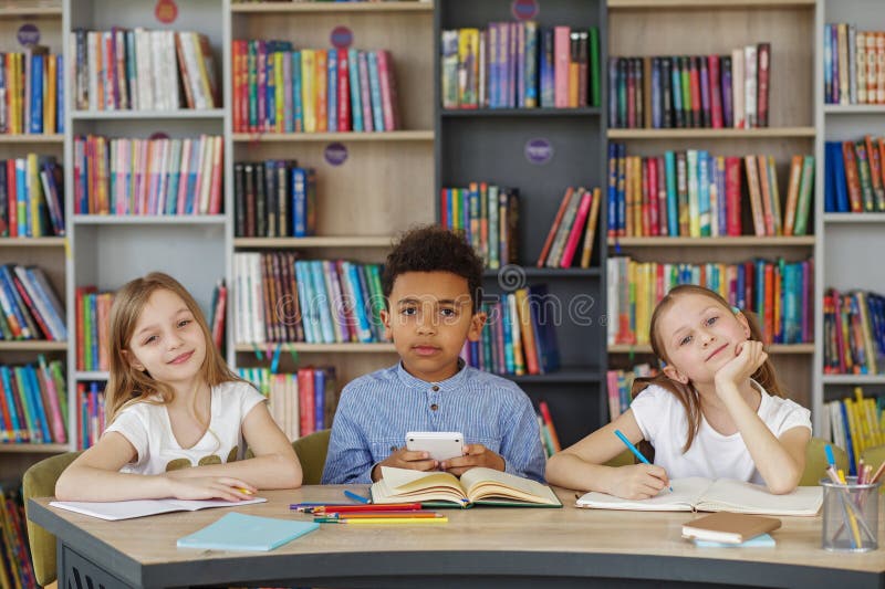 Multi-ethnic Pupils Study and Write at Table in Library or Classroom ...