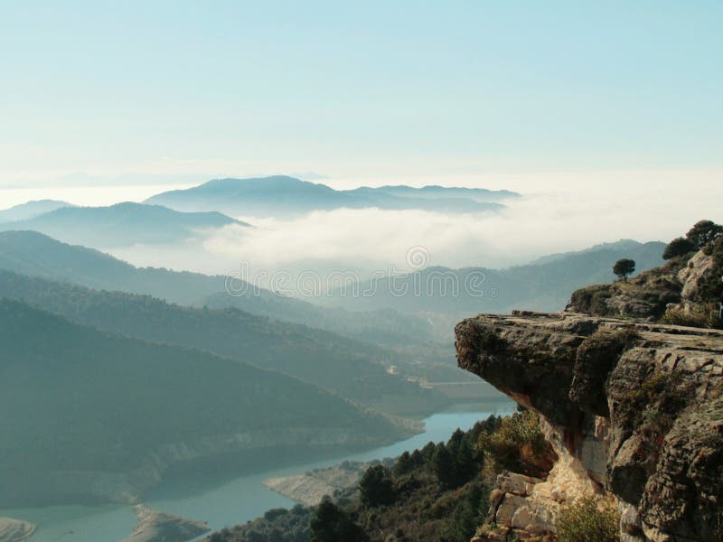 Cliff Next To the River with Mountains and Clouds in the Background ...