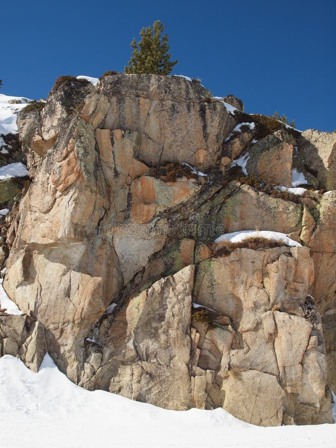 A Cliff on a Snowy Slope Against the Blue Sky with a Lone Tree on Top ...