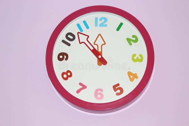 A Clock with Multi-colored Numbers on the Dial Hangs on a Pink Wall ...