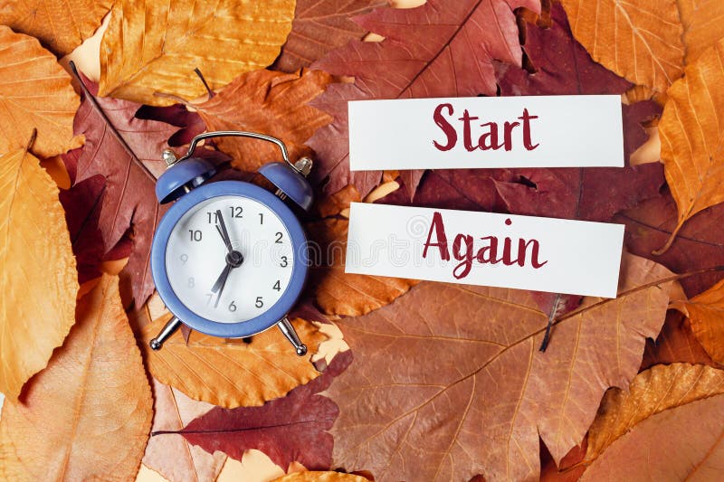 Clock is on a Pile of Leaves with the Words Start Again Written on Top ...