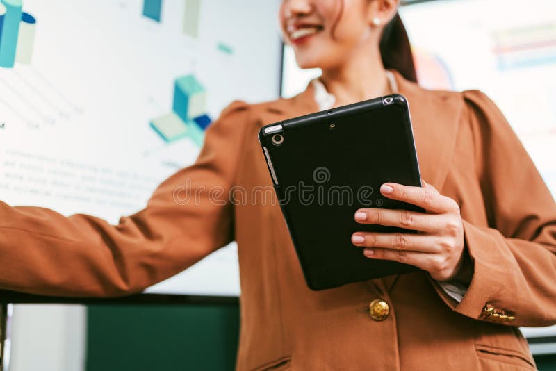 Close-up of Asian Businesswoman Using Tablet during Data Presentation. Smiling and Confident ...