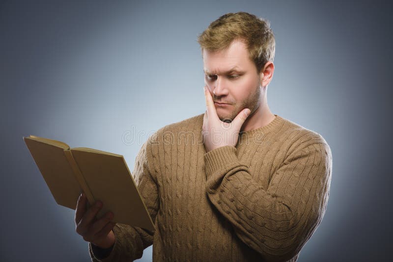 Close-up Of Confused Man Reading Book Against Gray Background Stock ...