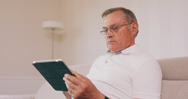 A Close-up of a Grandfather Using a Tablet Computer Man Sitting on Sofa ...