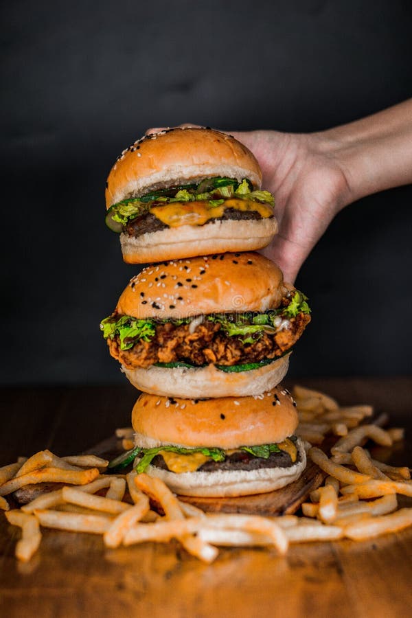 A Hand Holding a Stack of Three Cheeseburgers Stock Photo - Image of ...