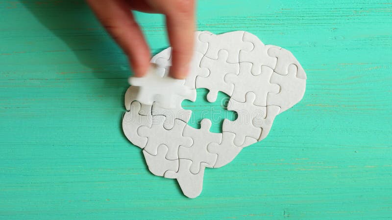 Hand Inserting Puzzle Piece into Brain-Shaped Puzzle on Teal Background ...