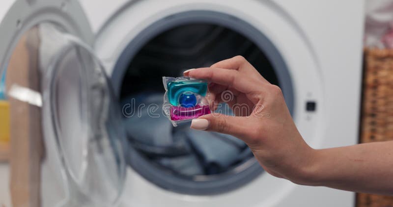 Close-up of Hands Holding a Laundry Capsule and Dropping it into the ...