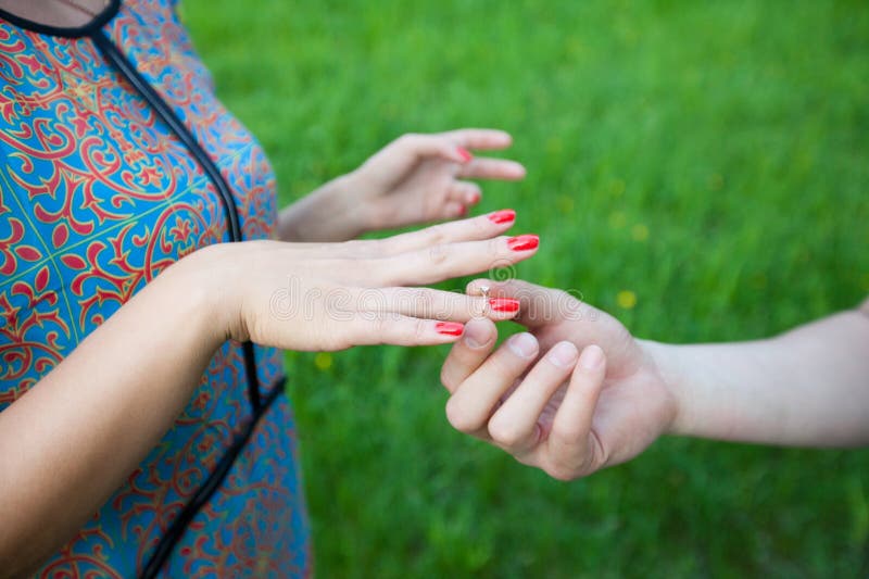 Close-up of Hands with Red Nails Exchanging Ring on Green Background ...