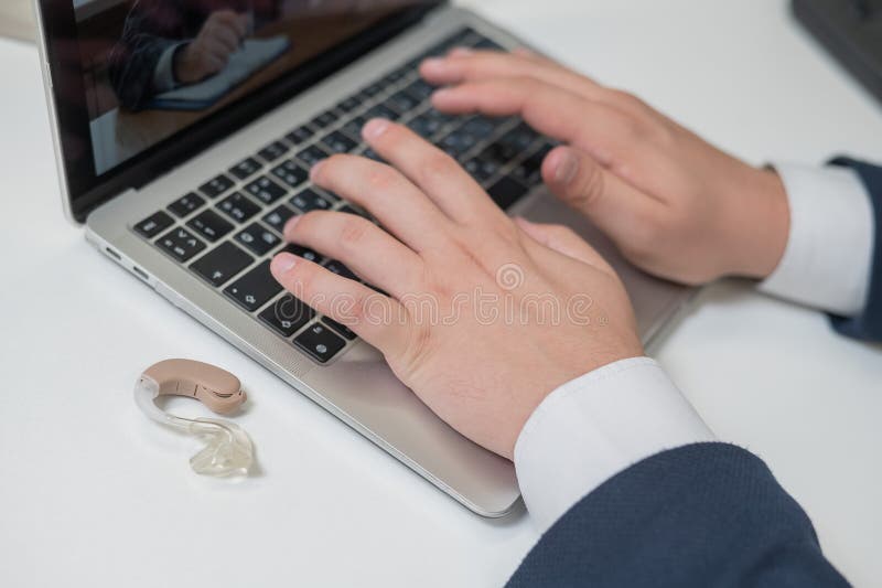 Close-up of a Man S Hands on a Laptop Keyboard. Hearing Aid on the ...