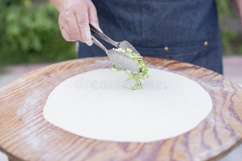 Old Female Cook Wearing Apron, Holding Spoons, Putting Filling on Dough ... Old Female Cook Wearing Apron, Holding Spoons, Putting Filling on Dough ...