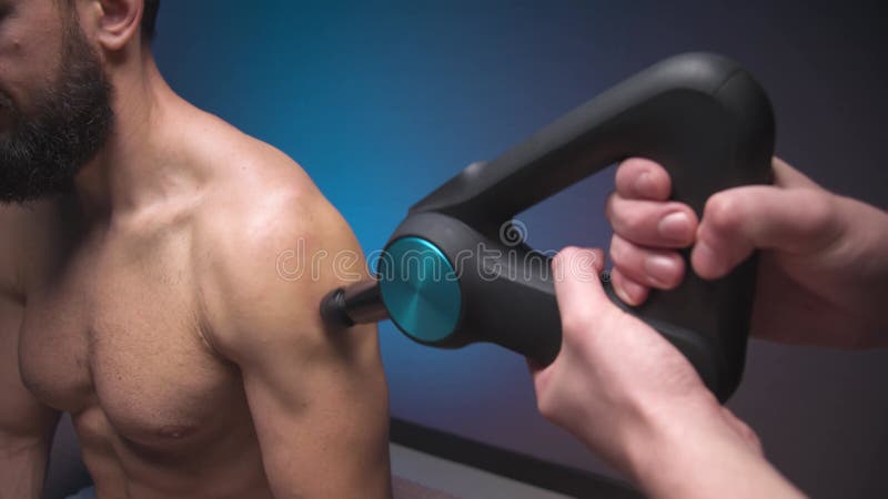 Close Up Percussion Massager In The Hands Of A Masseur Makes A Massage Of The Shoulders And