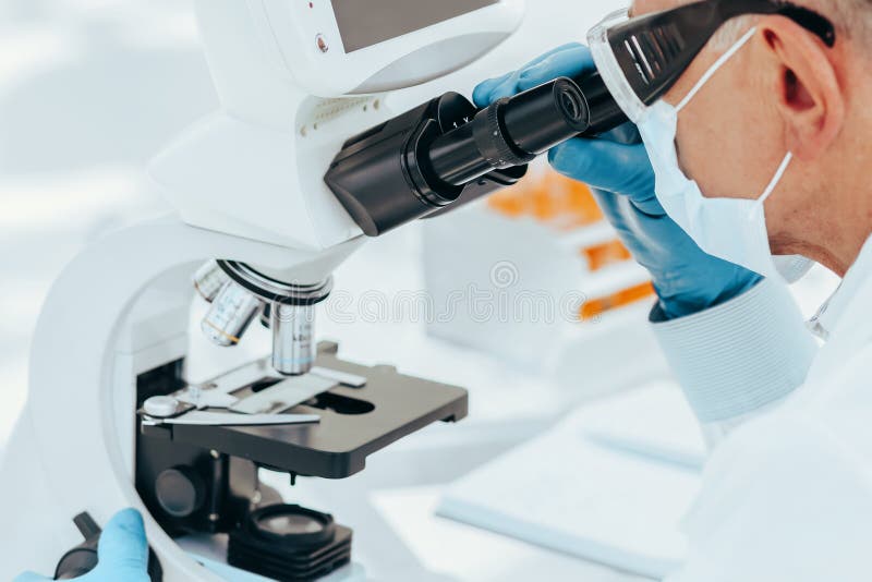 Scientist Biologist in a Protective Mask Looking through a Microscope ...