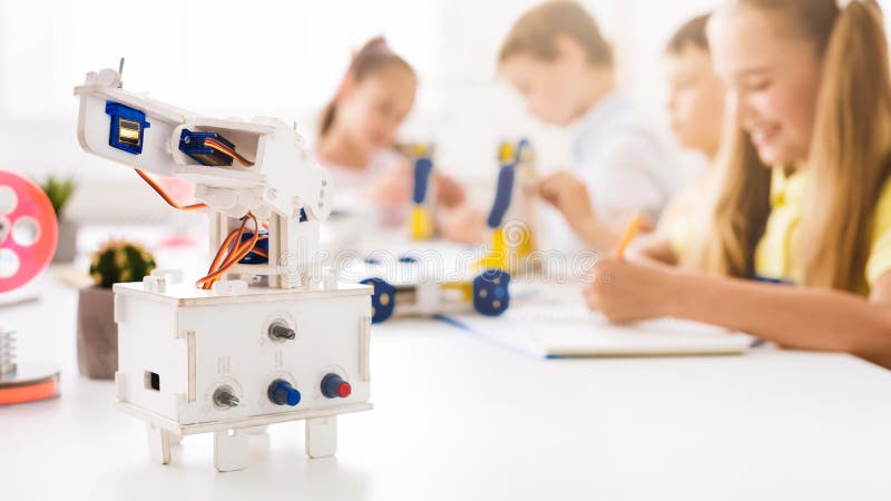 White Robotic Arm in Classroom Setting with Blurred Children Building ...