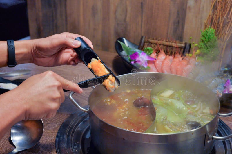 Hands Adding Orange Fish Roe Paste To a Steaming Hot Pot with Two ...