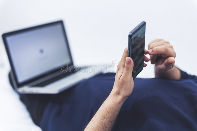 Close Up View of a Man Using His Mobile Phone and a Lap Top while Lying ...