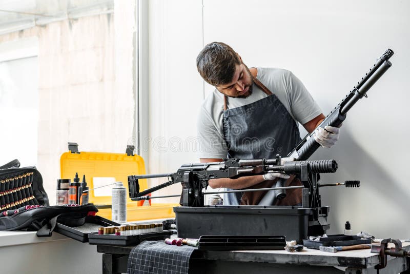 Close Up of Young Man in Apron Disassembling a Gun Above the Table ...
