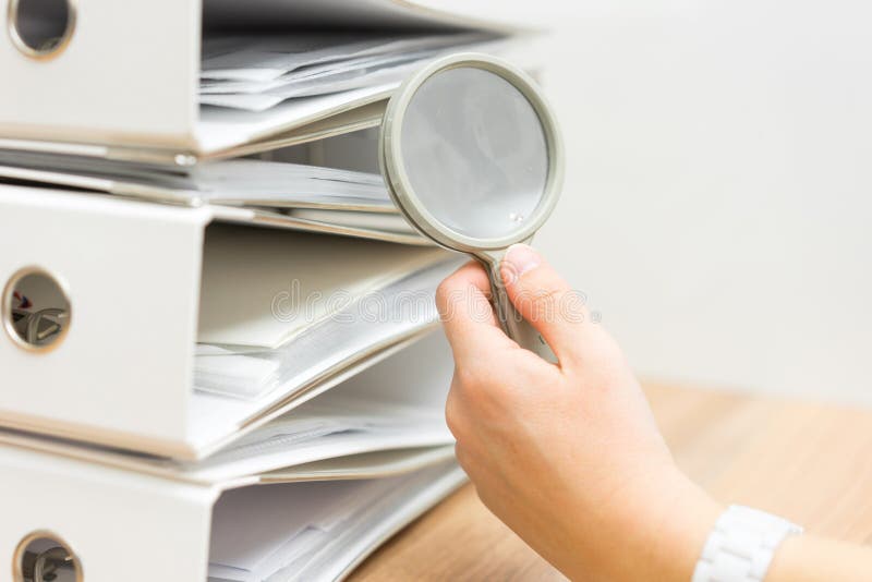 Closeup Of Hand Using Of Magnifying Glass To Inspect Stack Of Do Stock