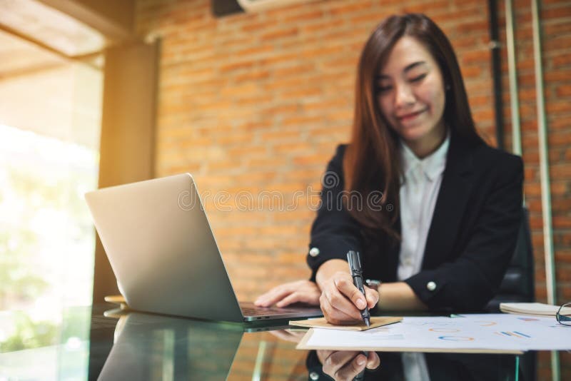 Business Woman Writing on Paperwork while Working on Laptop Computer in ...