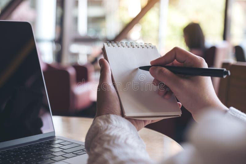 Hands Holding and Writing Down on a Blank Notebook with Computer Laptop ...