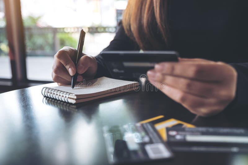 A Woman Holding a Credit Card while Writing Down on Notebook on Table ...