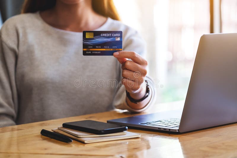 A Woman Holding Credit Cards while Using Laptop Computer in Office ...