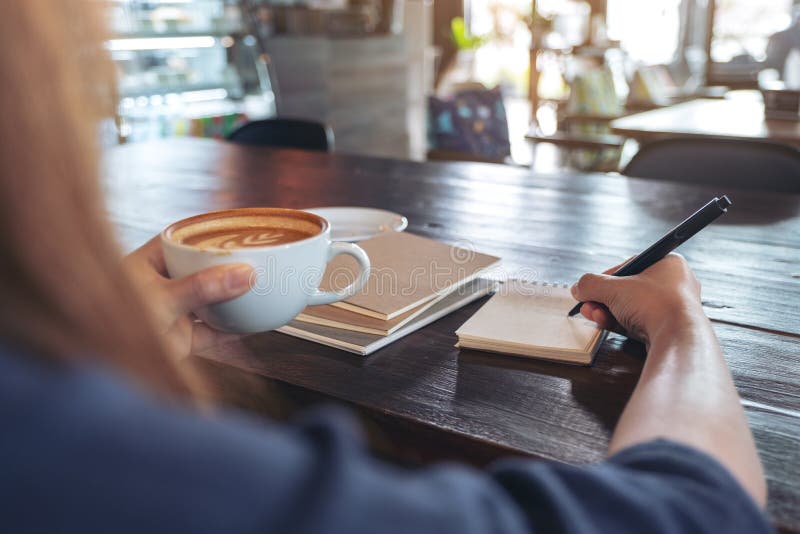 A Woman Writing on Blank Notebook while Drinking Coffee in Cafe Stock ...
