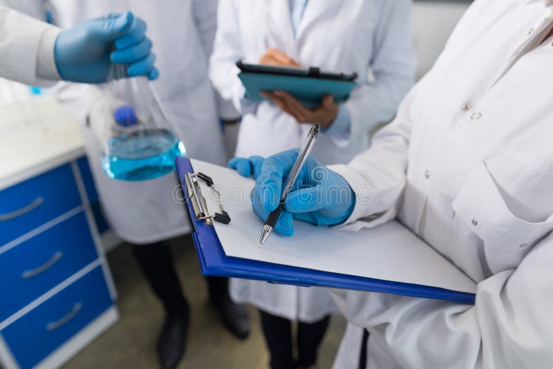 Closeup of Scientist Holding Flask and Group of Students Taking Notes ... Closeup of Scientist Holding Flask and Group of Students Taking Notes ...