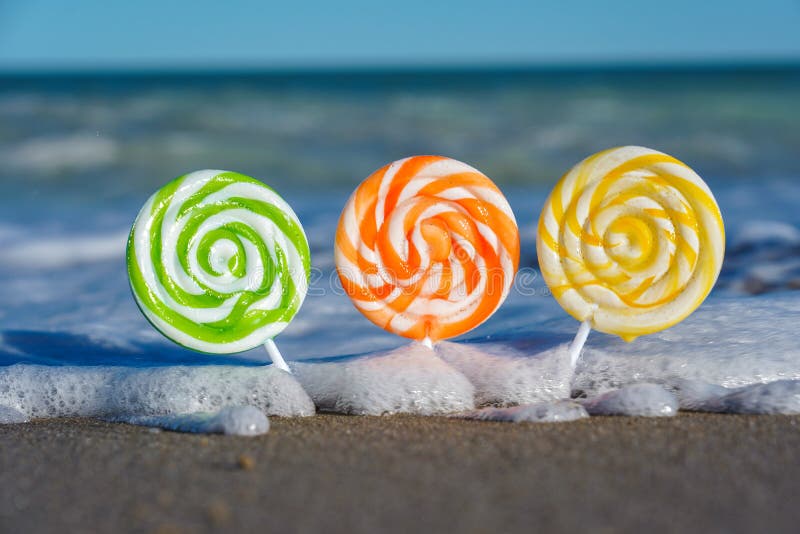 Closeup of Three Different Lollipops on a Beach Surrounded by the Sea ...