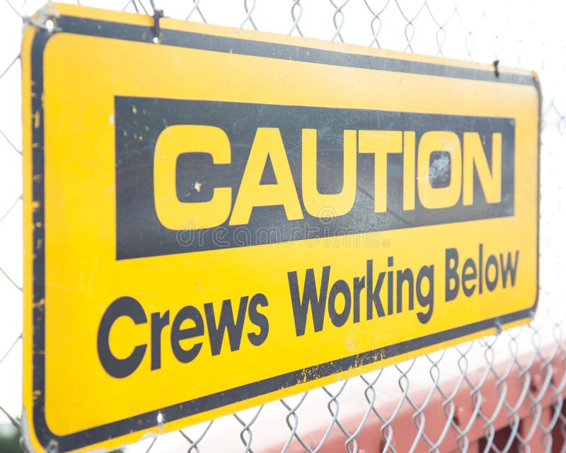 Closeup of a Yellow [Caution Crews Working Below] Sign on a Chain-link ...