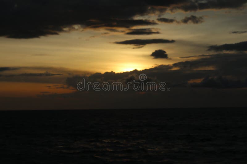 A Cloudy Sky Over the Ocean with a Dark Sky and the Sun Setting Behind ...