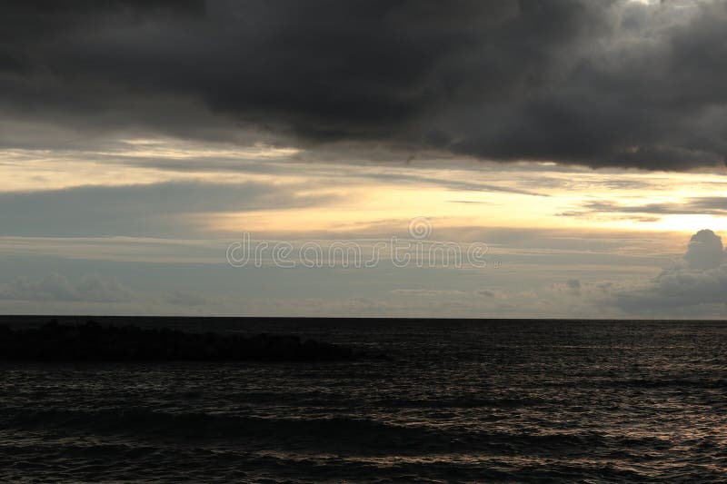 A Cloudy Sky Over the Ocean with a Dark Sky and the Sun Setting Behind ...